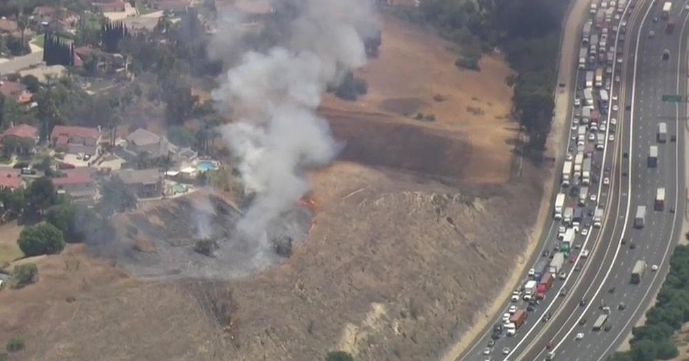 Crews extinguish brush fire burning in between homes, the 60 Freeway in ...